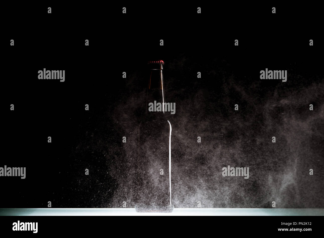 bottle of beer with spraying water around at table on black background ...