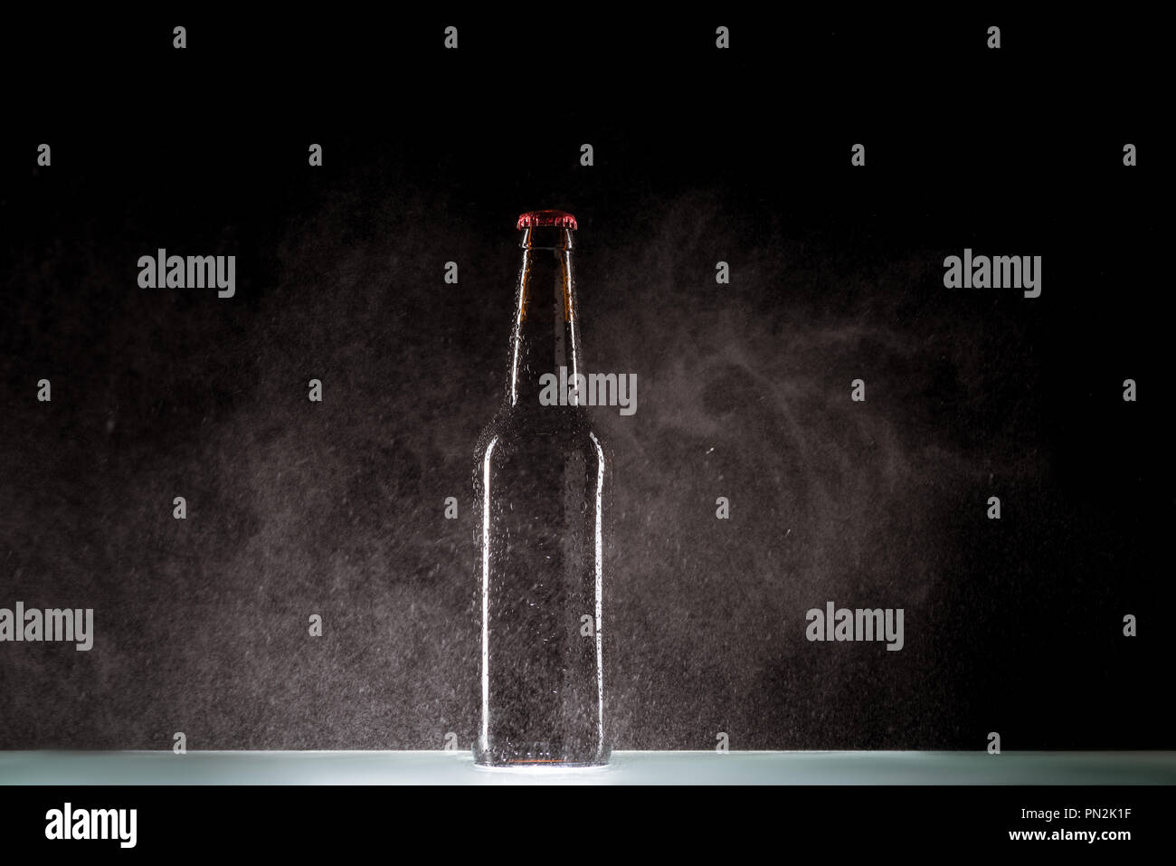 beer bottle with spraying water around at surface on black background ...