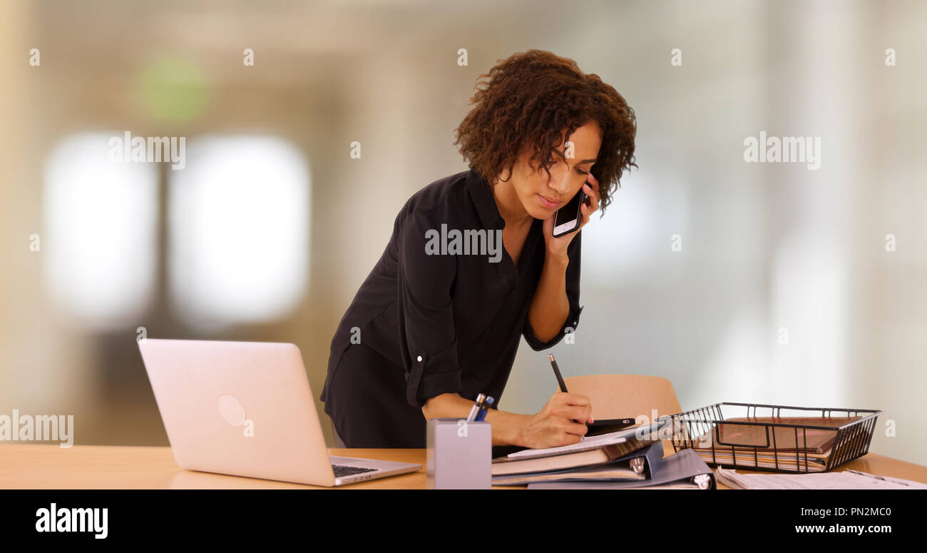Professional black woman multi-tasking on cell phone and laptop ...