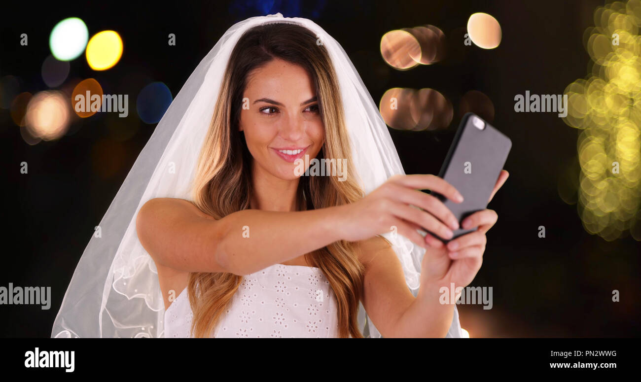 Young bride in wedding dress and veil taking a selfie with cell phone ...