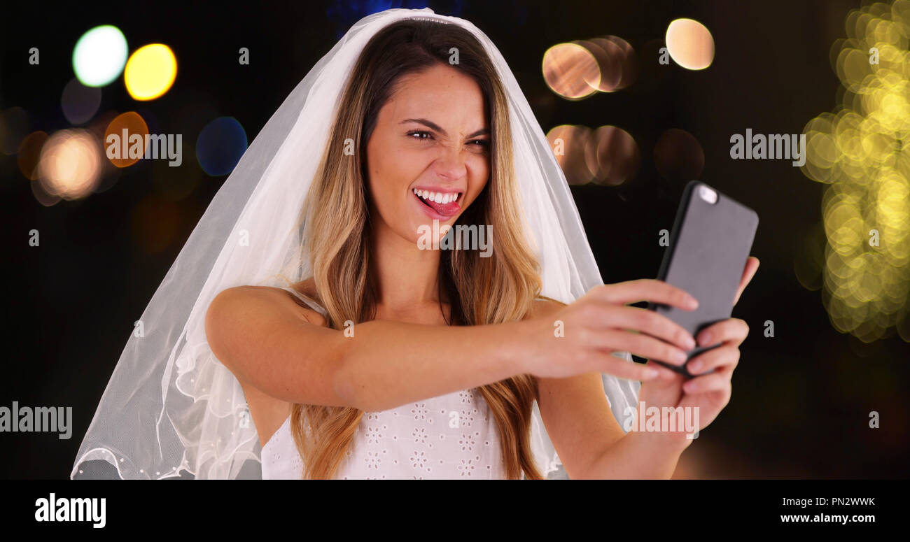 Young bride in wedding dress and veil taking a selfie with cell phone ...