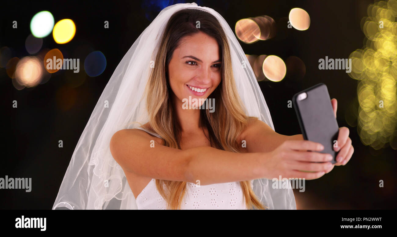 Young bride in wedding dress and veil taking a selfie with cell phone ...