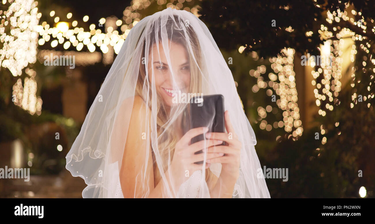 Young bride in wedding dress and veil taking a selfie with cell phone ...