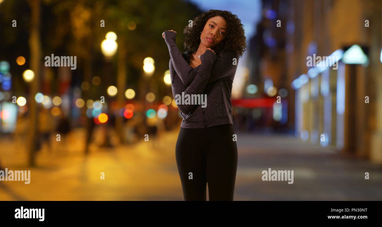 Portrait of black woman athlete on city street at night stretching ...