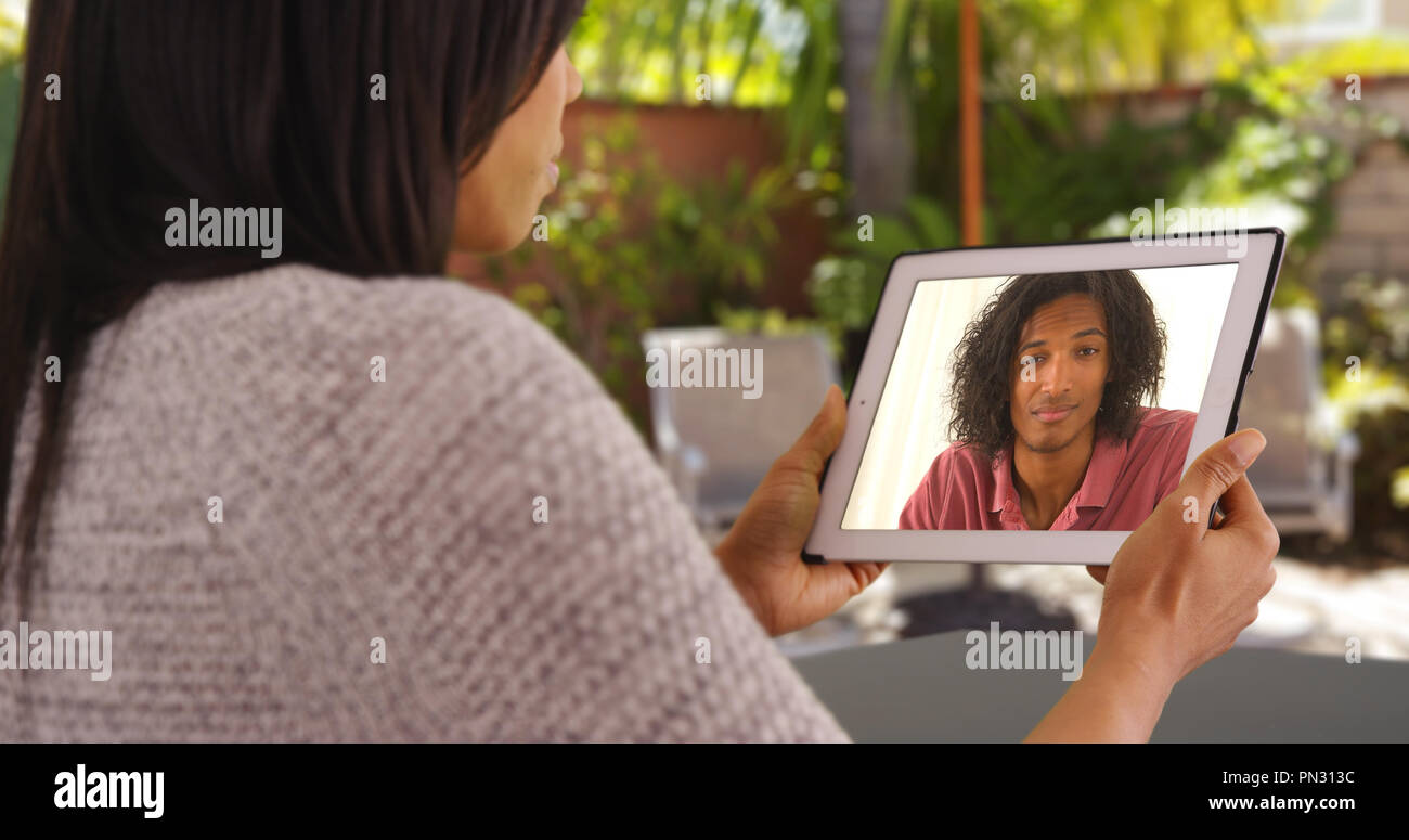 Over the shoulder shot of black woman video chatting male friend with ...