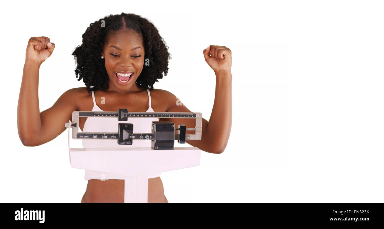 Attractive black woman happily weighs herself on scale in studio with ...