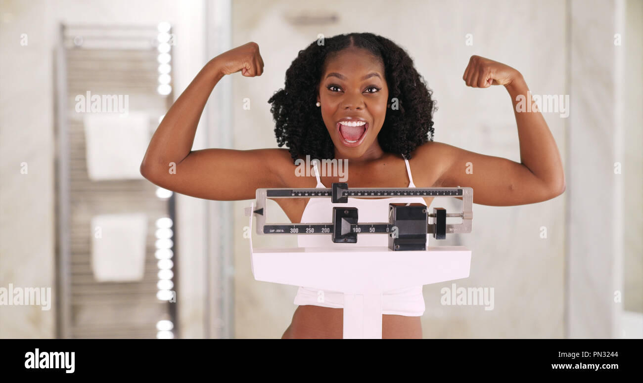 Smiling black woman stands on weight scale cheering and showing off ...