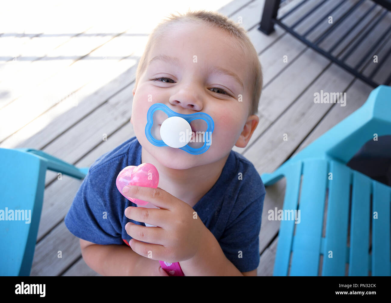 Two year old boy smiling through his pacifier and holding a heart ...