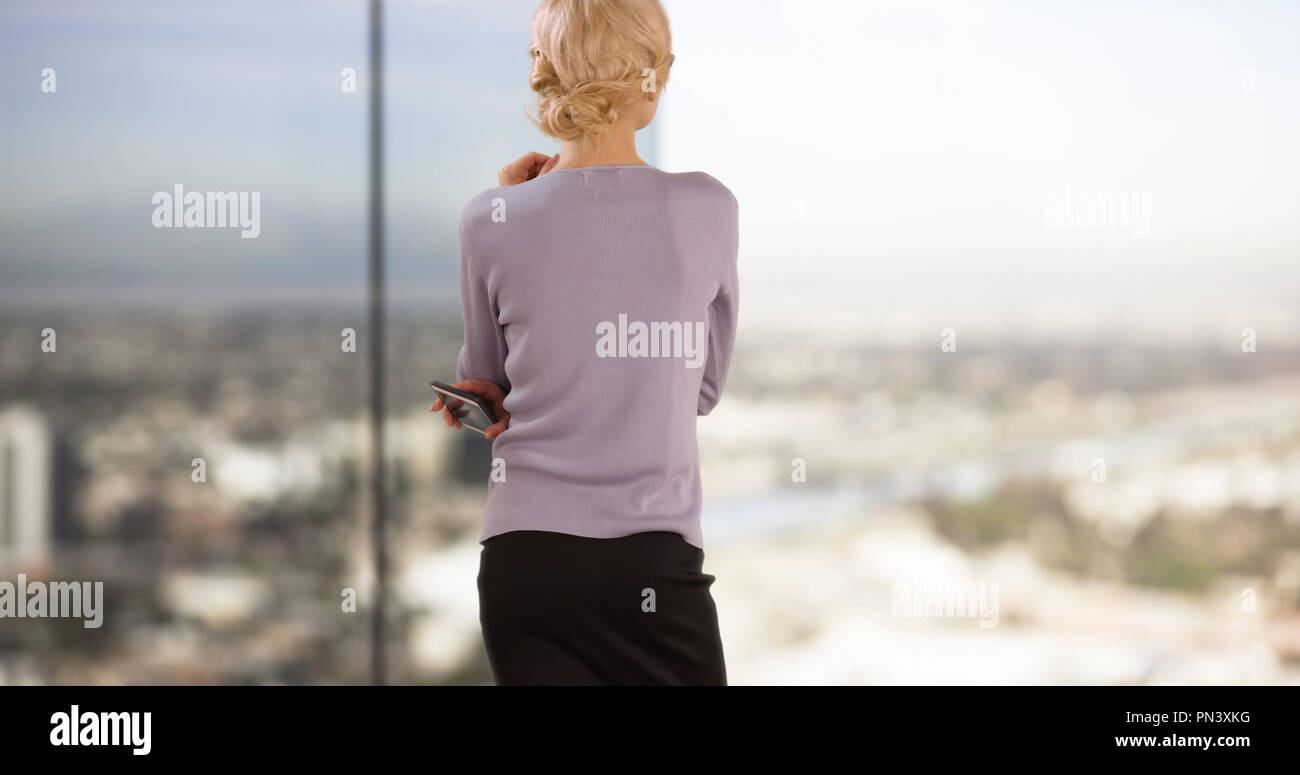 Female CEO standing back to camera enjoying view of the city from ...