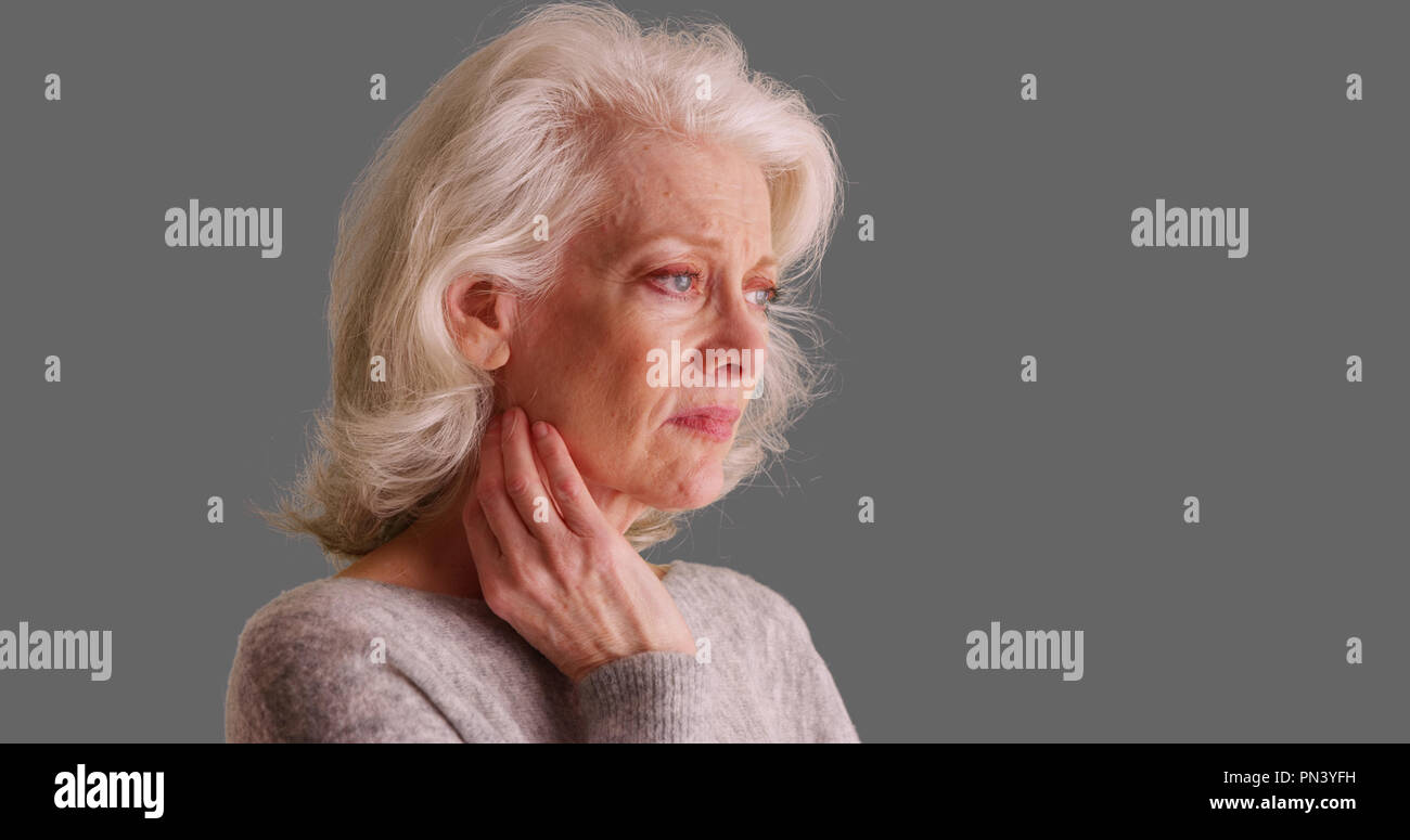 Mournful Caucasian female in her 50s looking concerned on gray backdrop ...