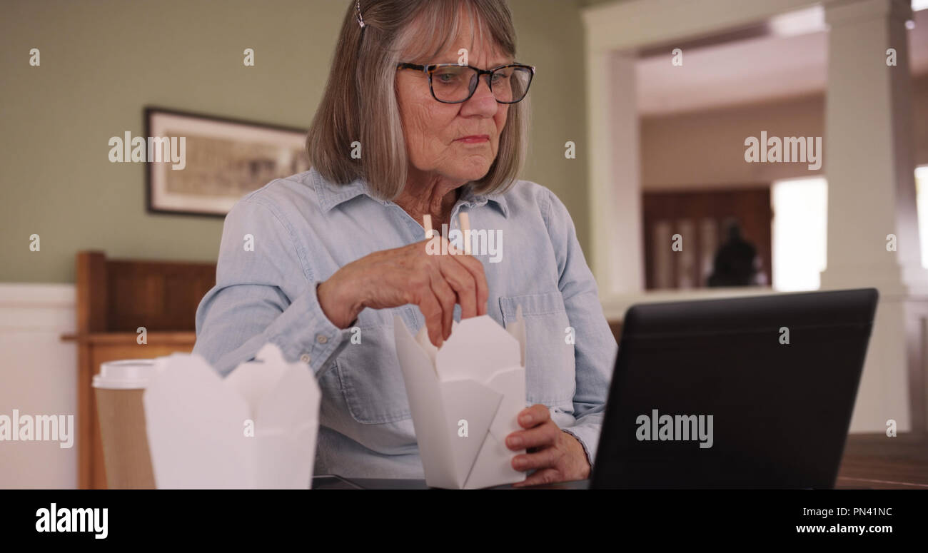 Retired senior woman having lunch and using laptop computer inside her ...