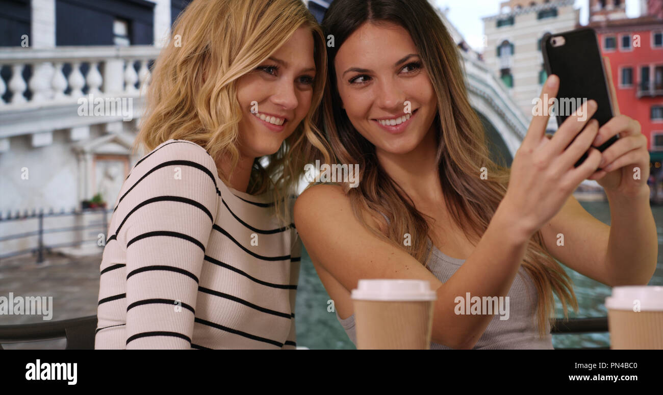 Two friends being social and using cell phone to take selfie by ...