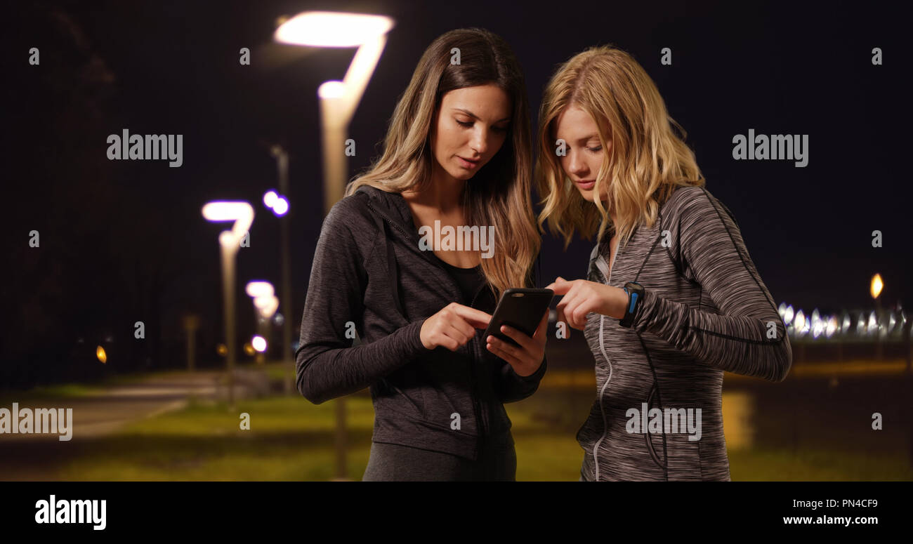 Two attractive women timing jog with stop watch and smartphone outside ...