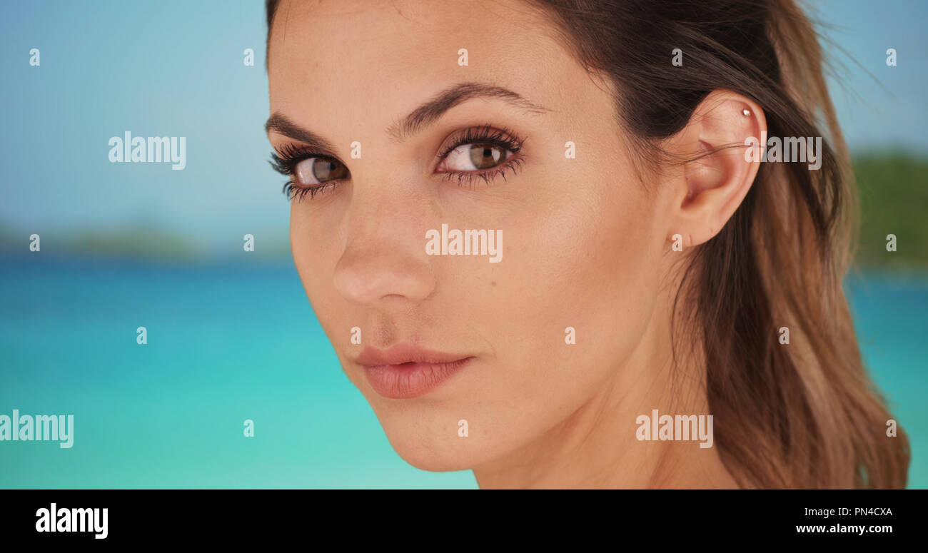 Pretty young lady facing camera staring with view of the ocean behind ...
