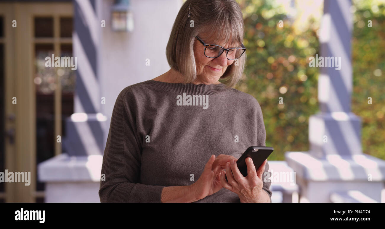 Happy senior woman sending text message on phone outside in the daytime ...