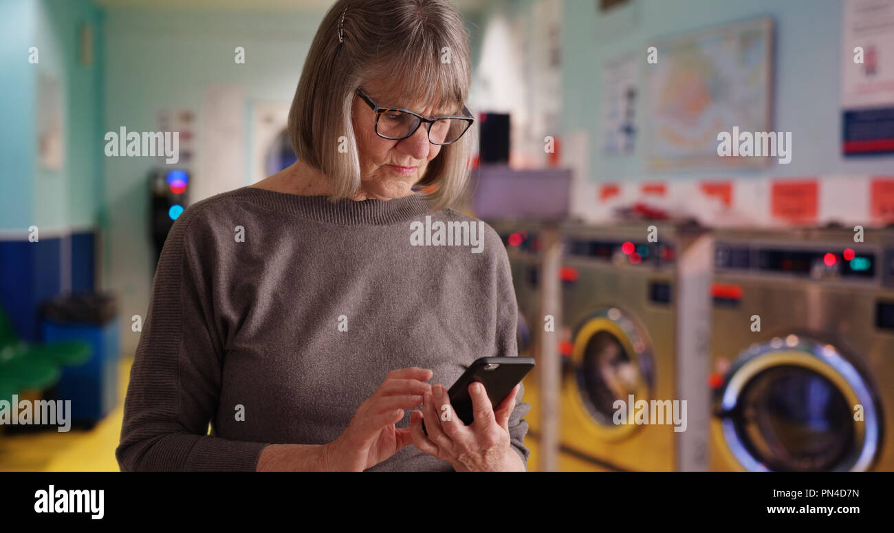 Somber old lady reading distressing news alone at laundromat Stock ...