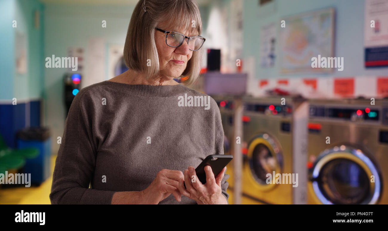 Somber old lady reading distressing news alone at laundromat Stock ...