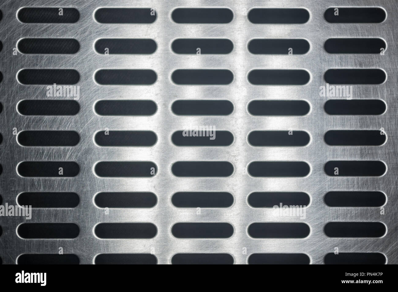 stainless steel grating with oblong holes on black background, close-up ...