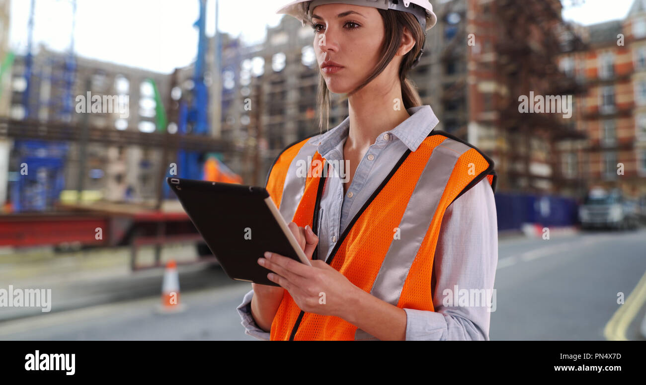 Focused female construction worker at work on pad device at ...