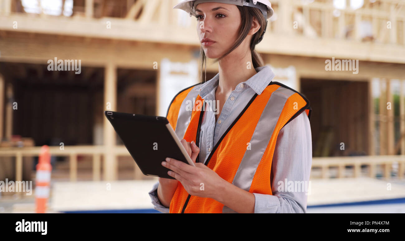Focused female construction worker at work on pad device by unfinished ...