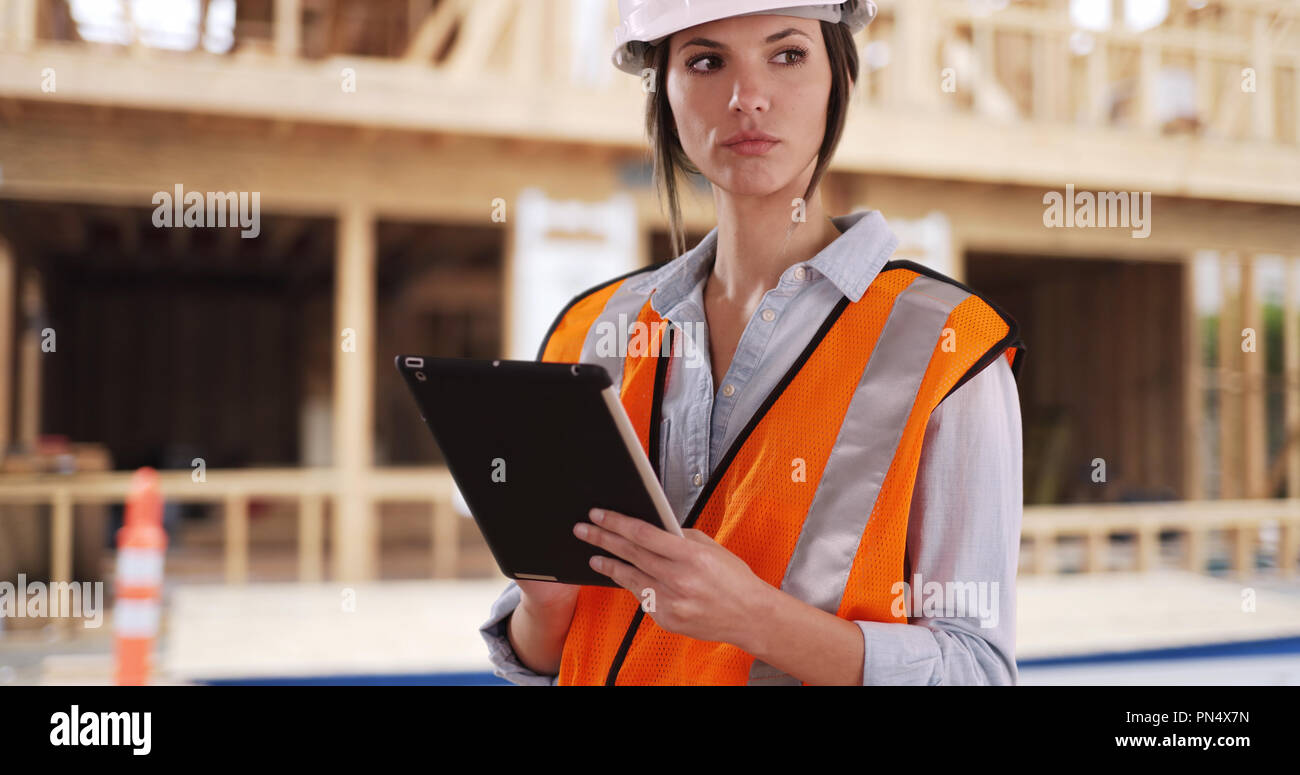 Focused female construction worker at work on pad device by unfinished ...