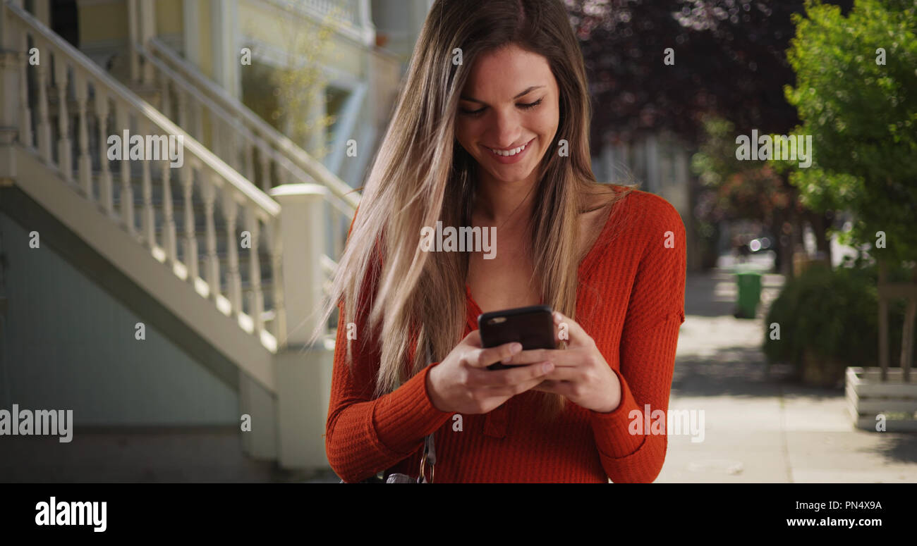 Millennial woman texting on smartphone looking happy in residential ...