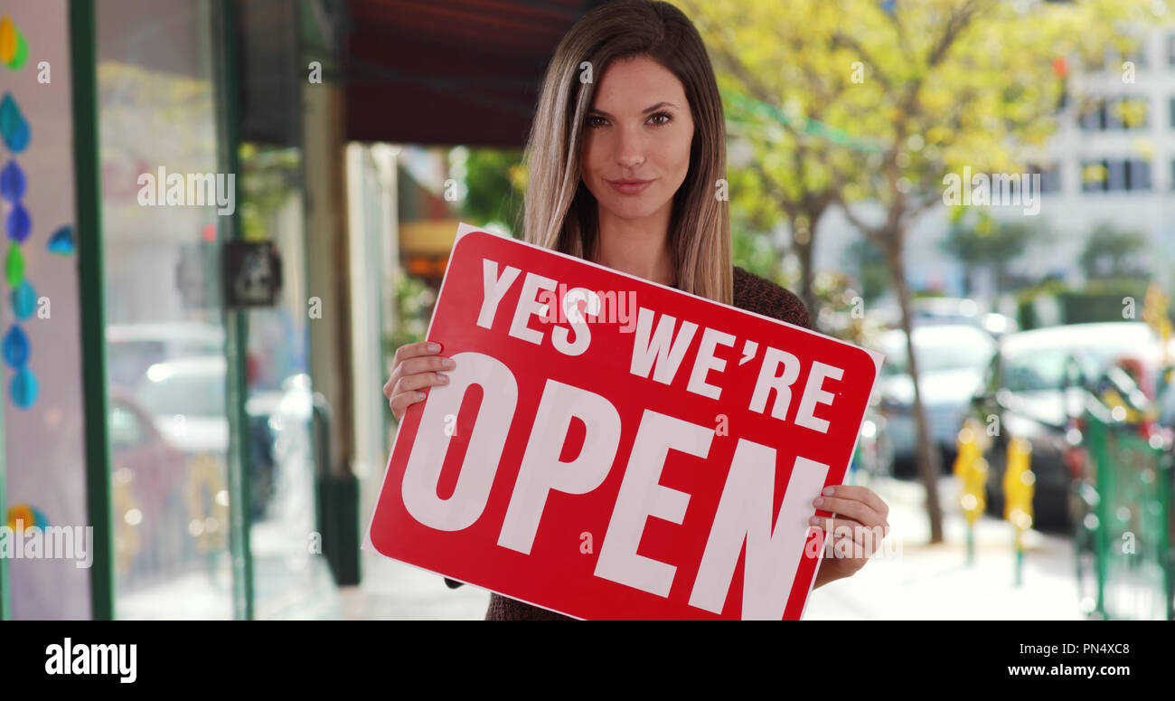 Small business owner holding Open Sign looking at camera outside her ...