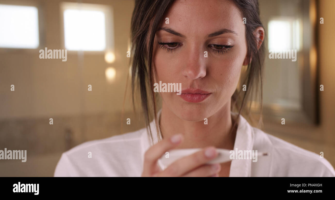 Caucasian female checking for fever inside her bathroom with ...