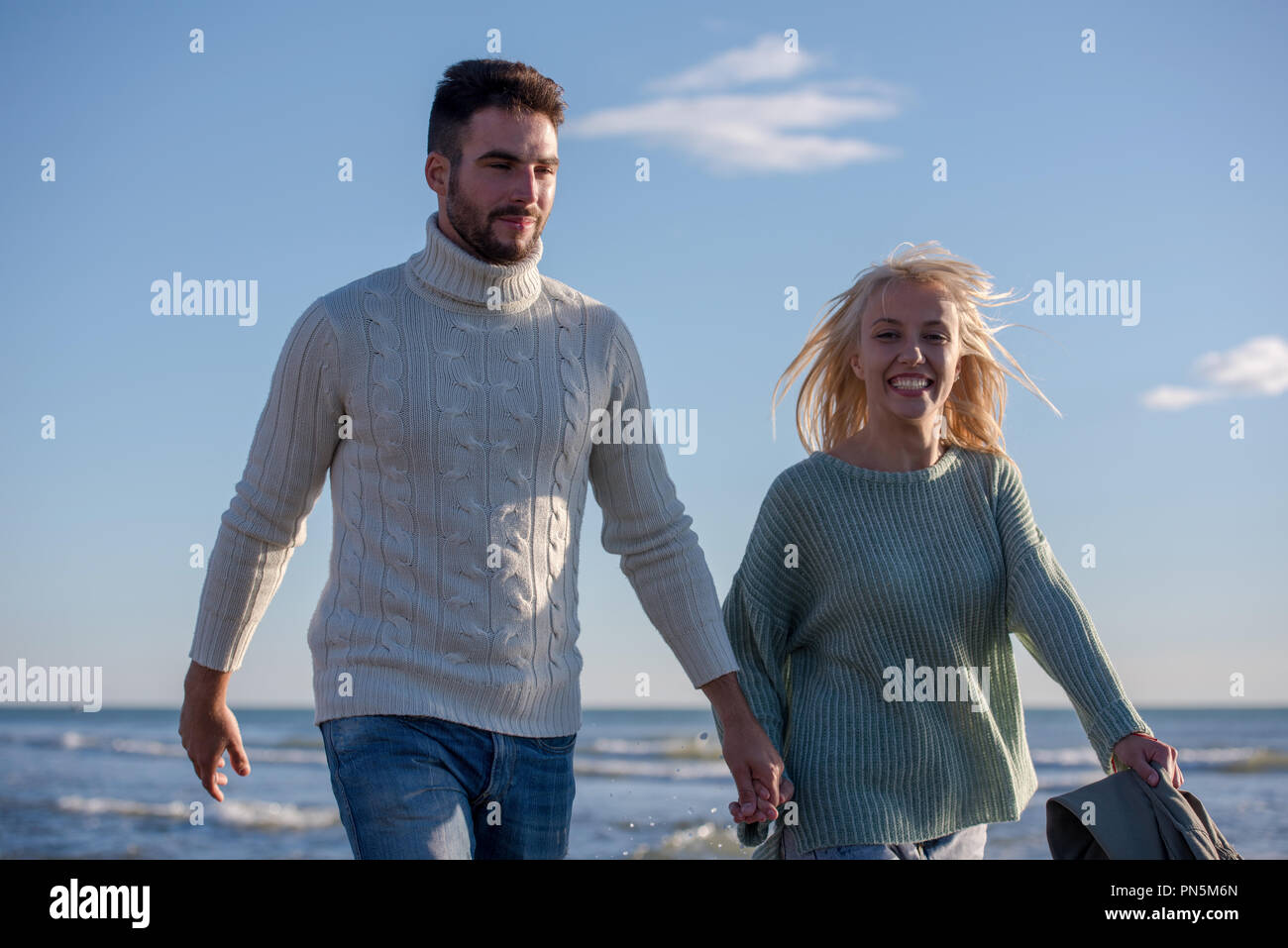 Young couple having fun walking and hugging on beach during autumn ...