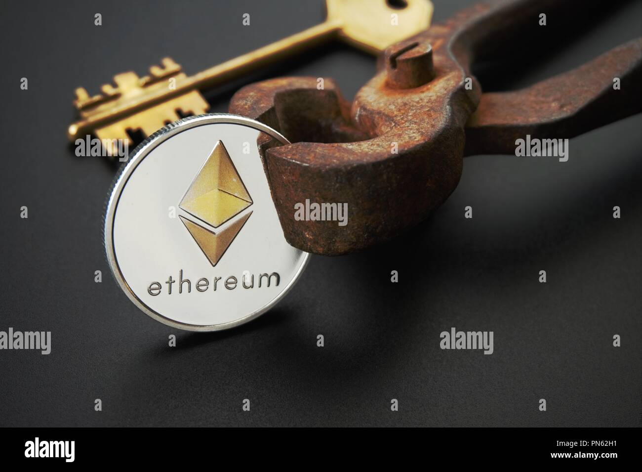 Close up of sheeny Ethereum coin and golden key on rusty vintage ...