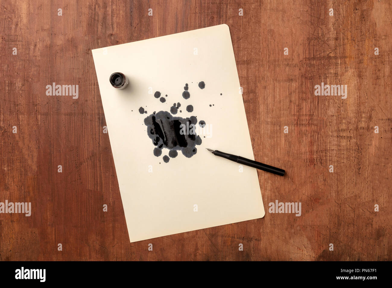 An overhead photo of an ink well with drops of ink and a nib pen, with ...