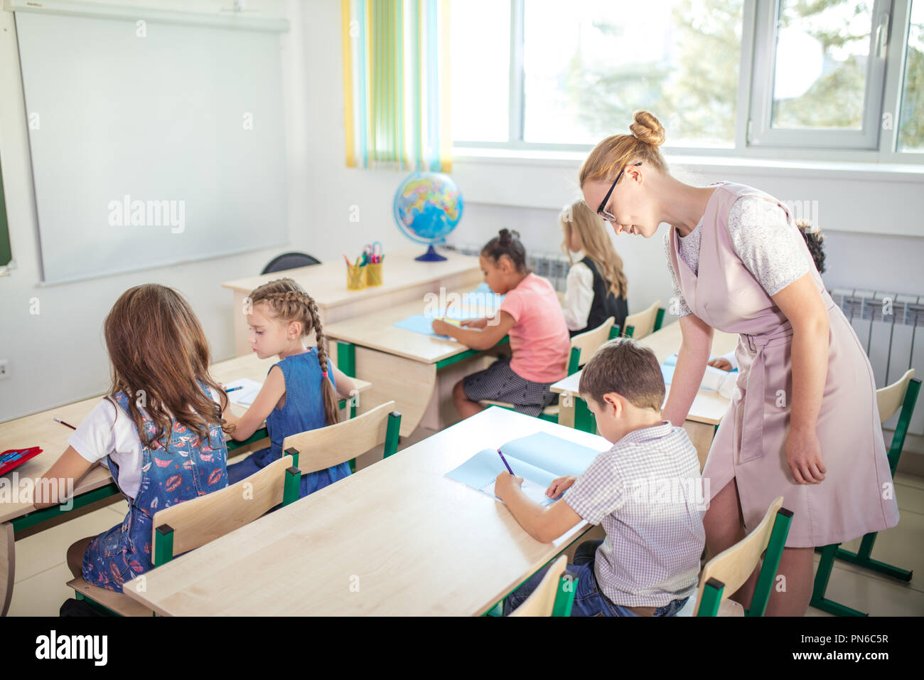 Teacher helping kids with their homework in classroom at school Stock ...