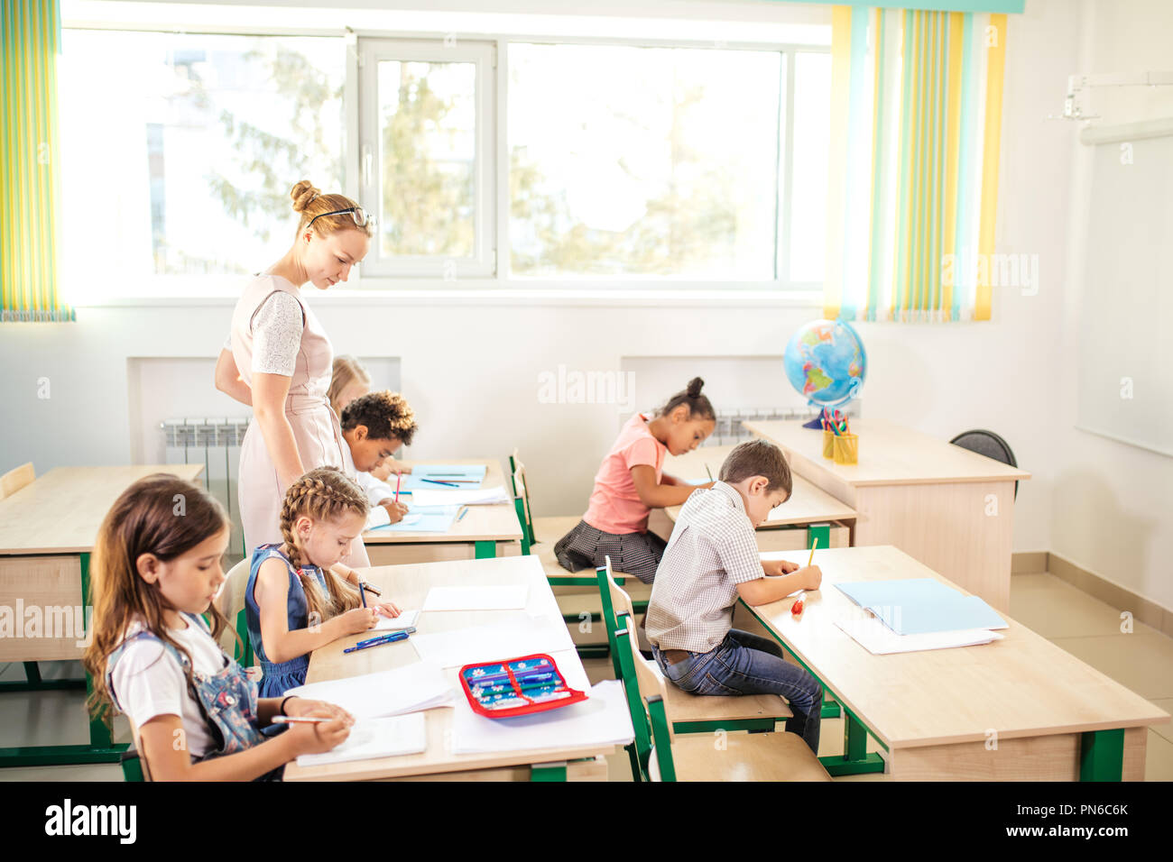 Teacher helping kids with their homework in classroom at school Stock ...