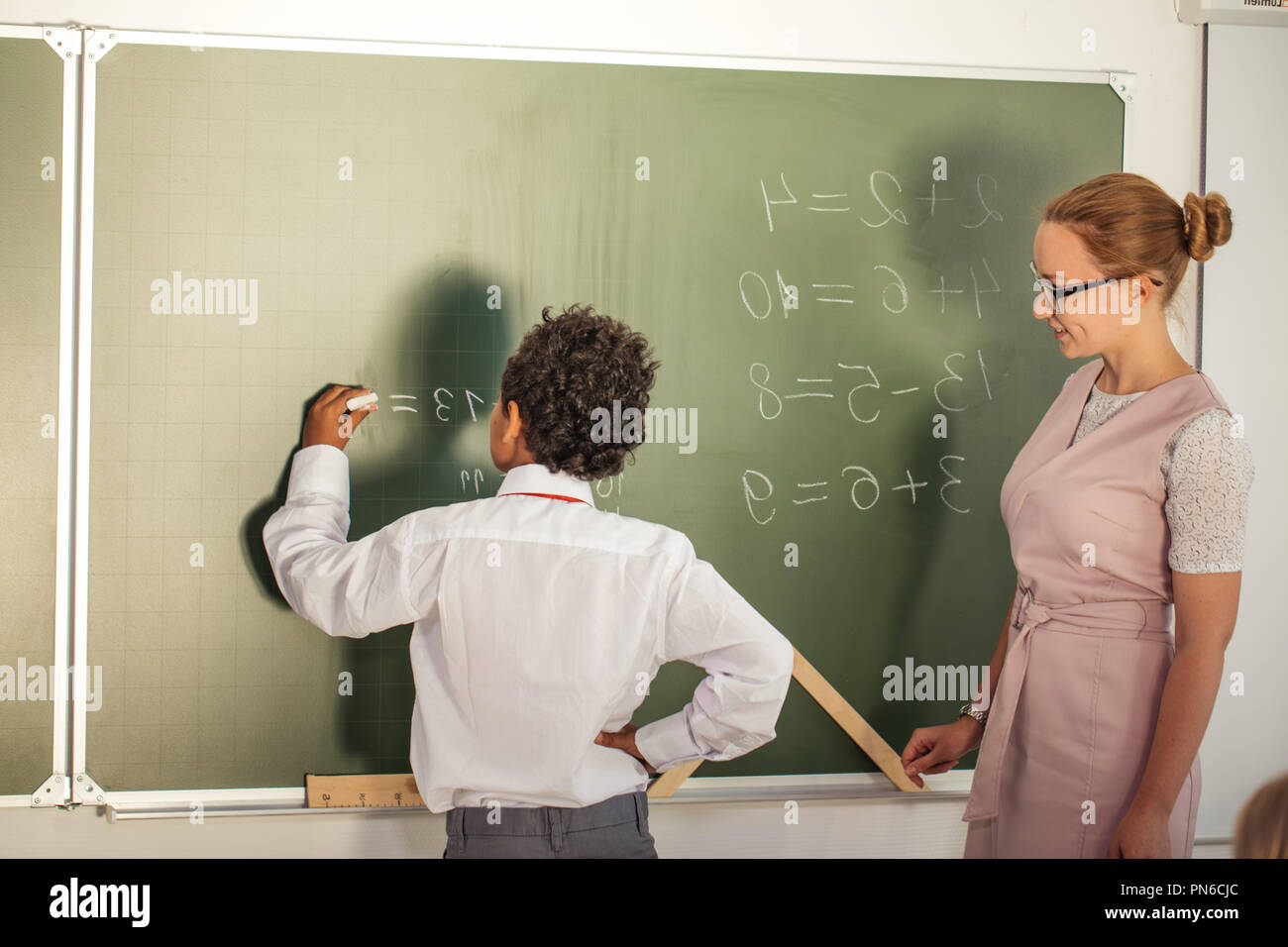 boy solving addition and subtraction on board. schoolboy writing ...