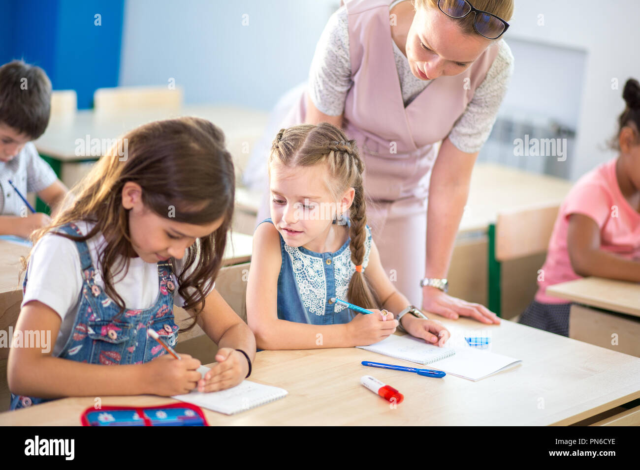 Teacher helping kids with their homework in classroom at school Stock ...
