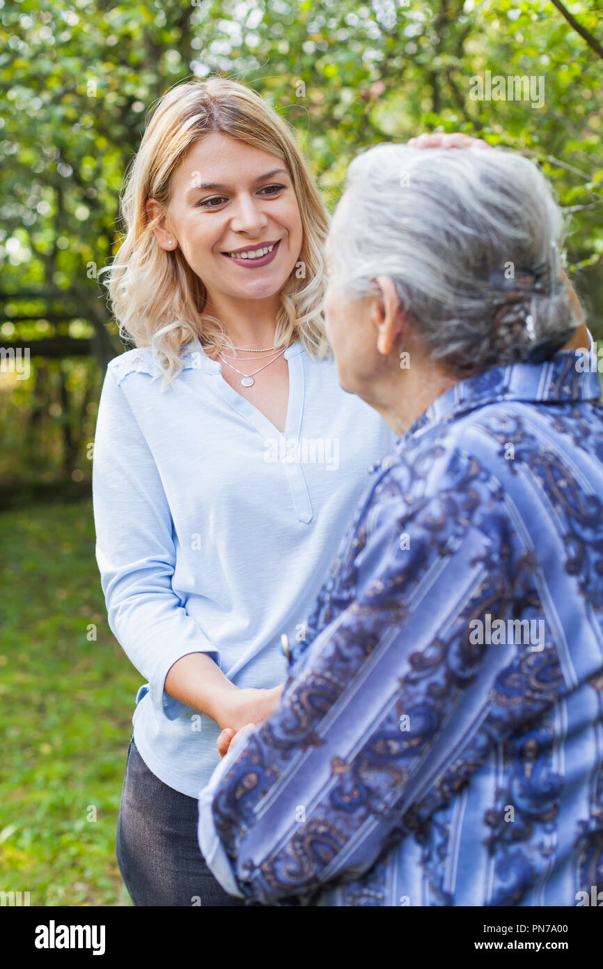 Friendly caregiver walking with old lady in the garden - Medical care ...