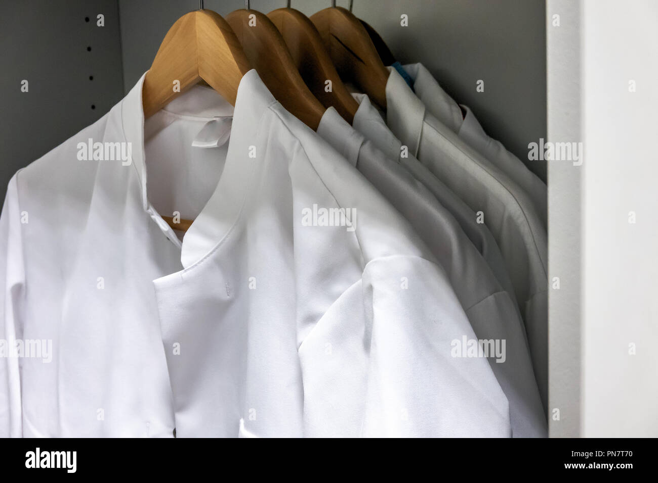 White smocks on wooden hangers hang in the cupboard of a laboratory ...