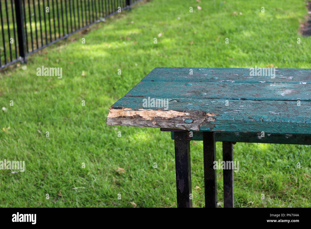 Rotten and damaged green painted wooden picnic bench top with a metal ...