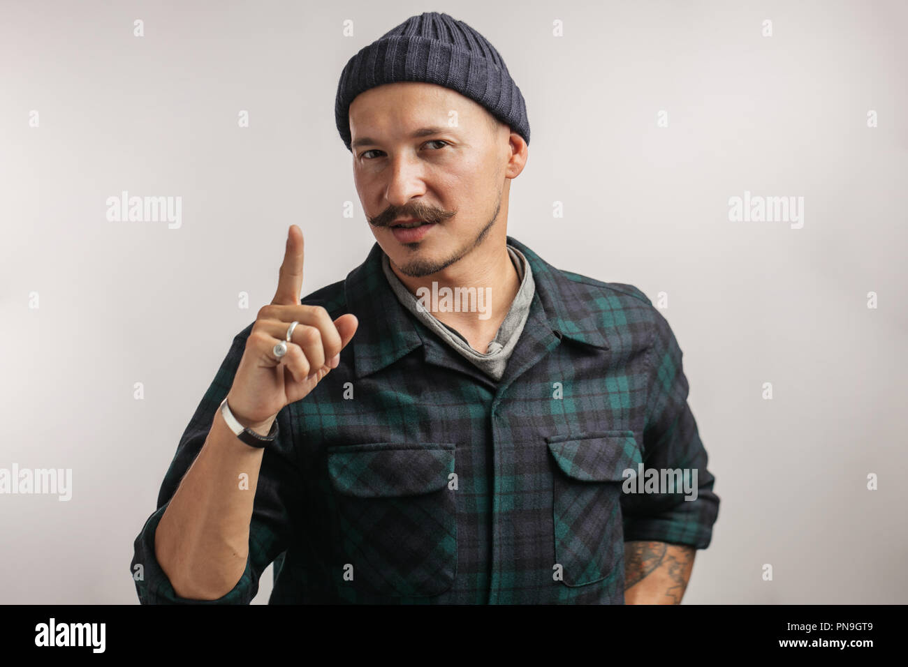 Confident man in knitted hat pointing finger upwards over white ...