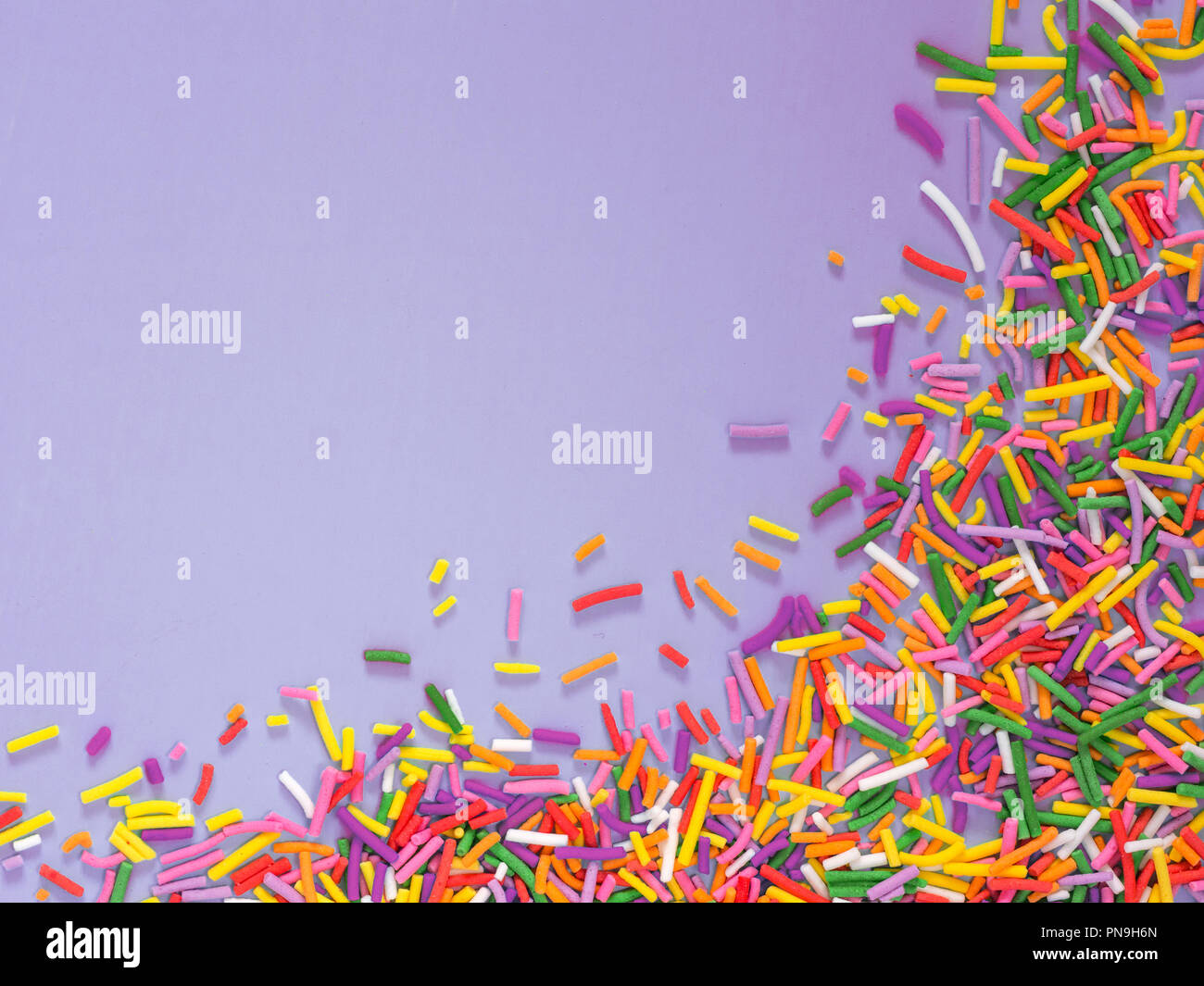 Border frame of colorful sprinkles on lilac purple background with ...