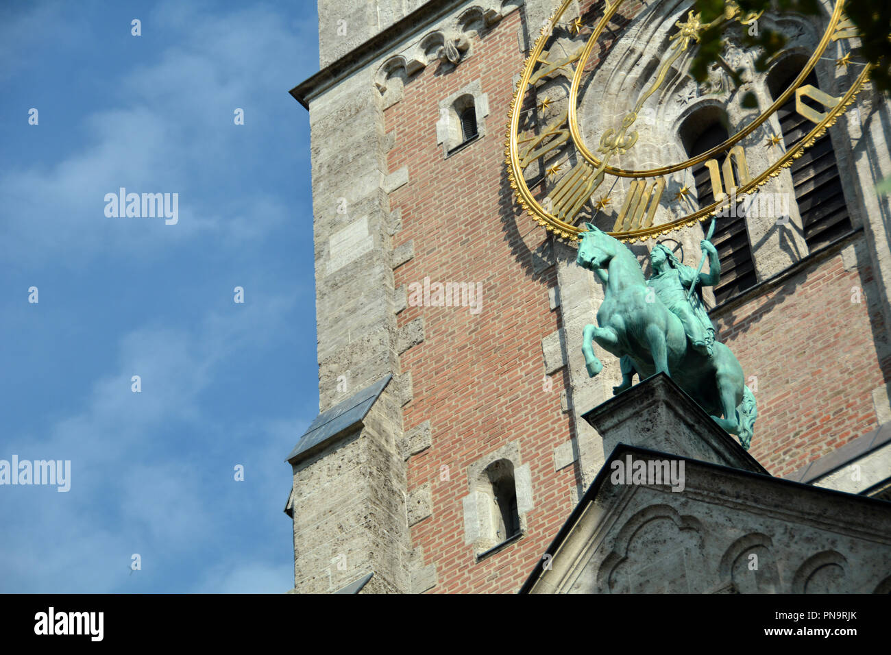 Green copper statue from below in front of a golden clock face with a ...