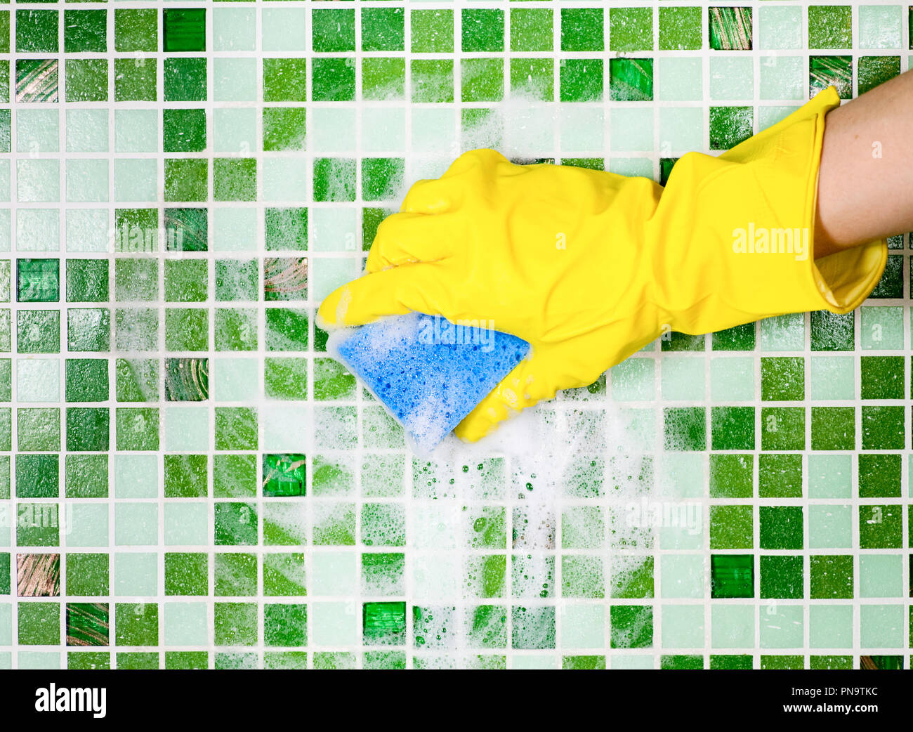 Hand in yellow protective glove cleaning mosaic wall Stock Photo - Alamy