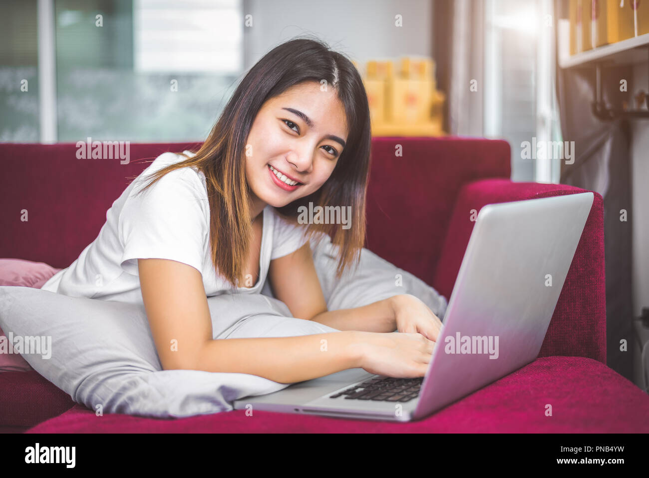 Young woman surfing the internet by laptop on red sofa in cheerful ...