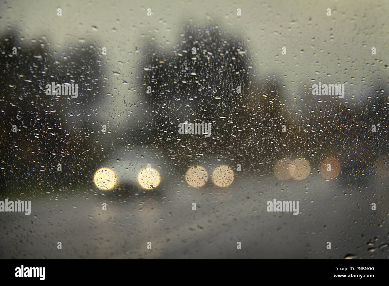 Cars with headlights on viewed through a raindrop-covered windshield ...