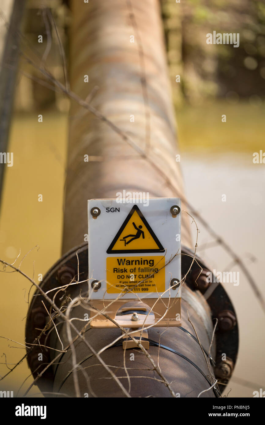 A warning sign on a pipe over a river next to a bridge warning not to ...