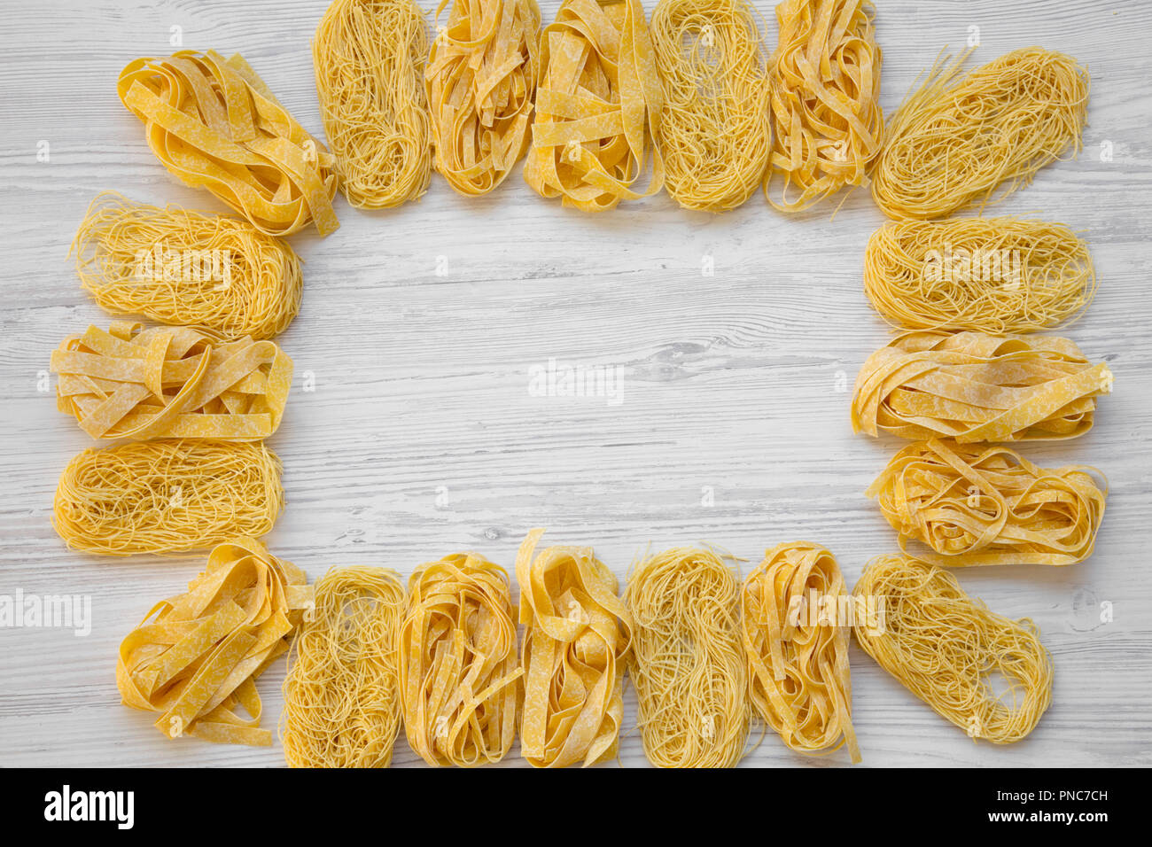 Frame of various uncooked pasta on white wooden background, overhead ...