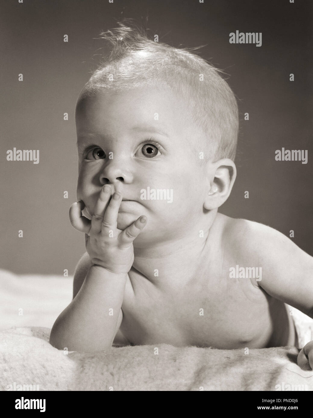 1960s PENSIVE FIVE MONTH OLD BABY LYING ON STOMACH LEANING CHIN IN HAND ...