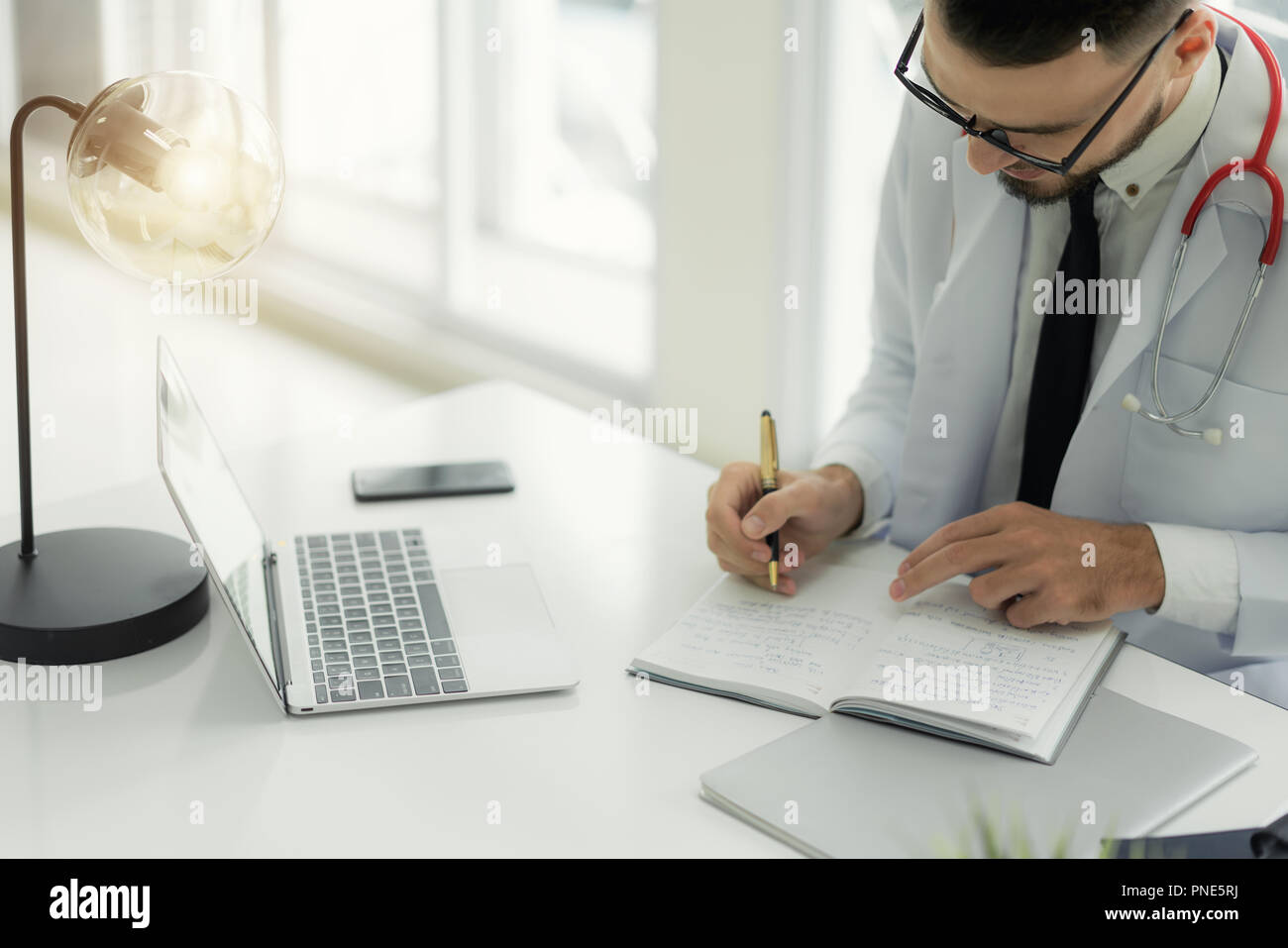 Doctor working with laptop computer and writing on paperwork with ...