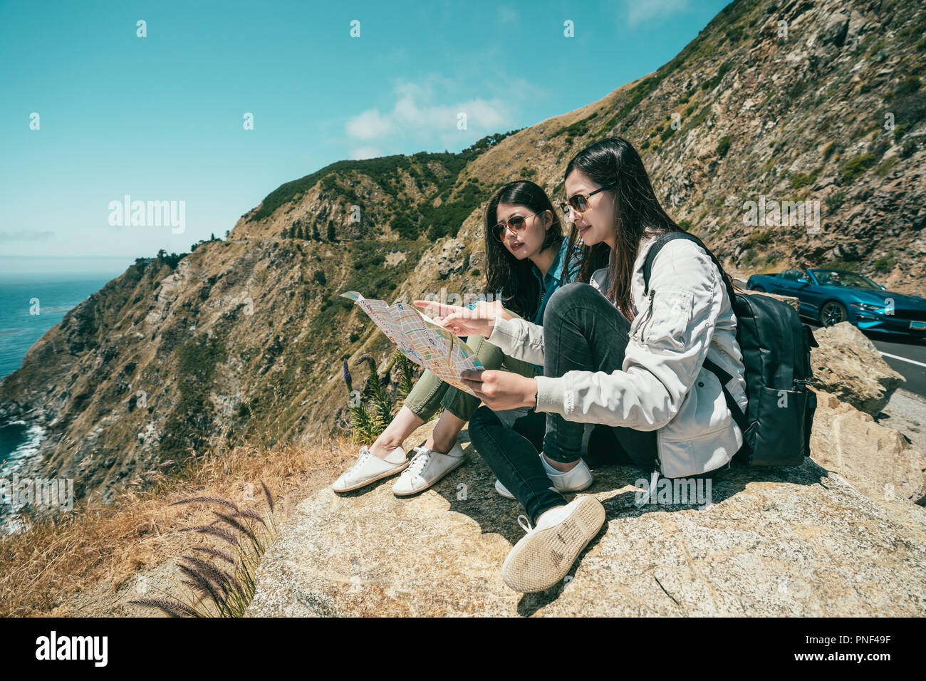 two young girls reading the guide map and sitting on the cliff while a ...
