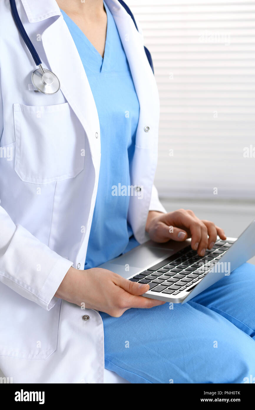 Woman doctor typing on laptop computer while working in hospital office ...